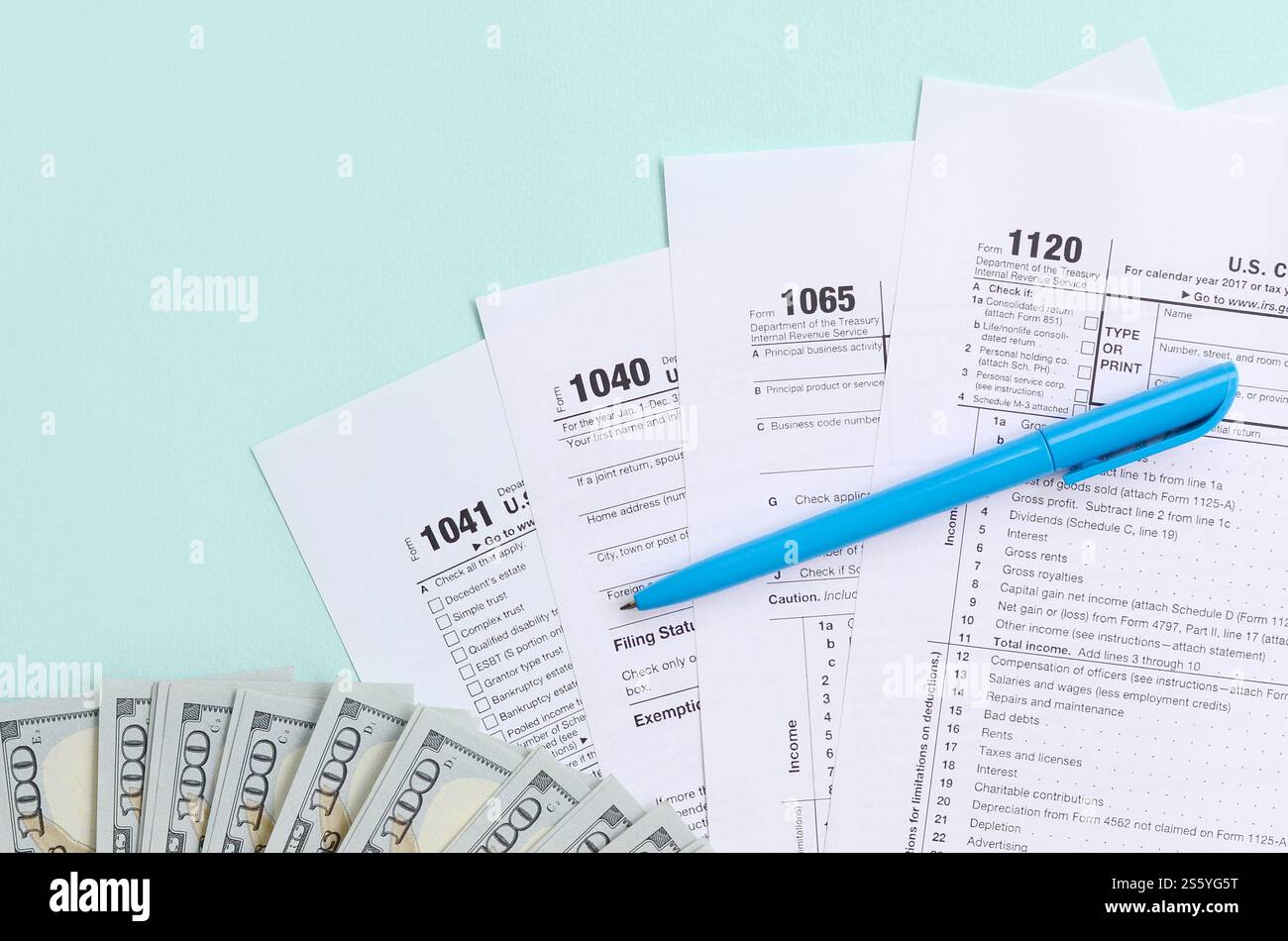 Tax forms lies near hundred dollar bills and blue pen on a light blue background. Income tax ...