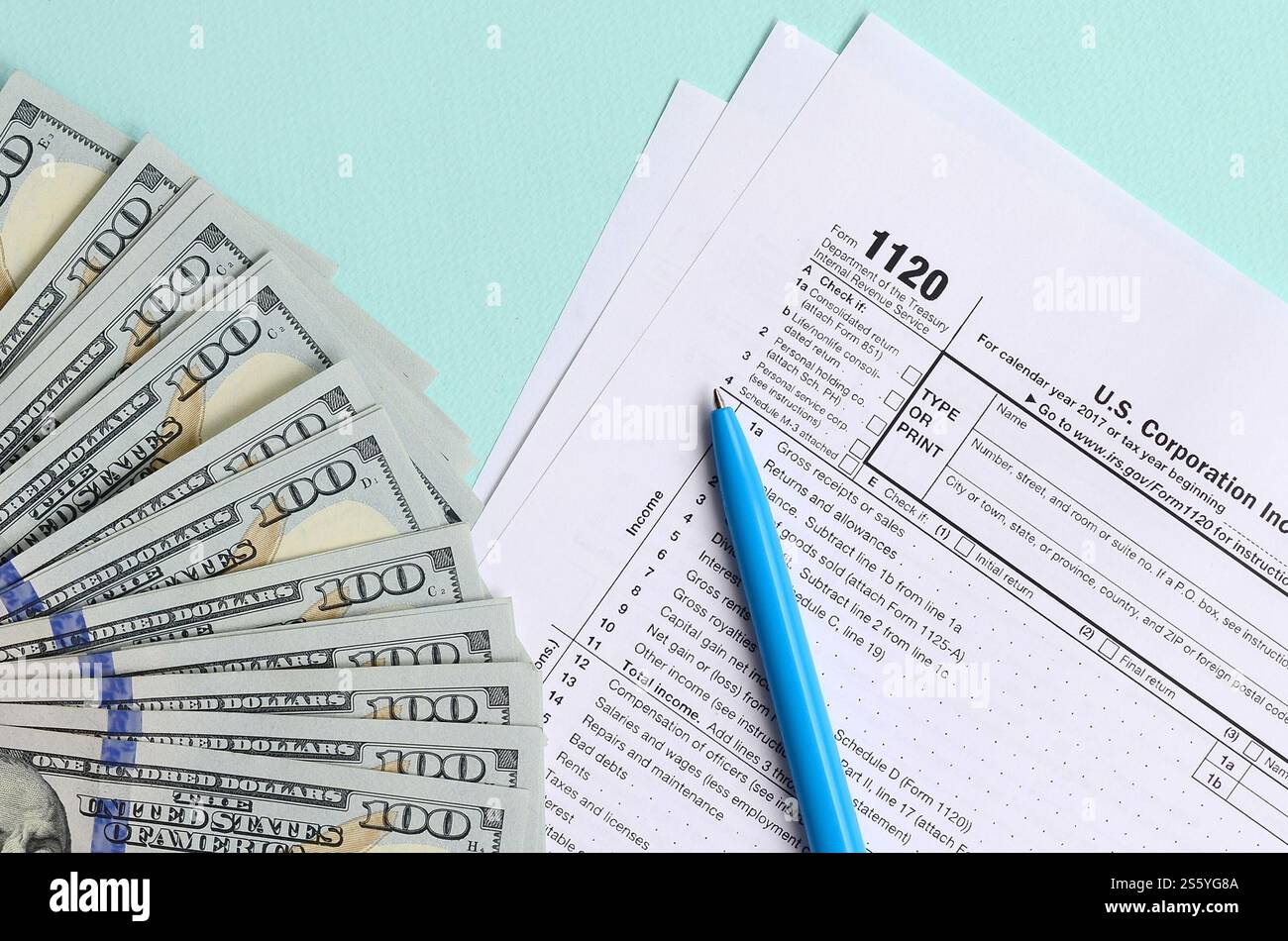 1120 tax form lies near hundred dollar bills and blue pen on a light ...