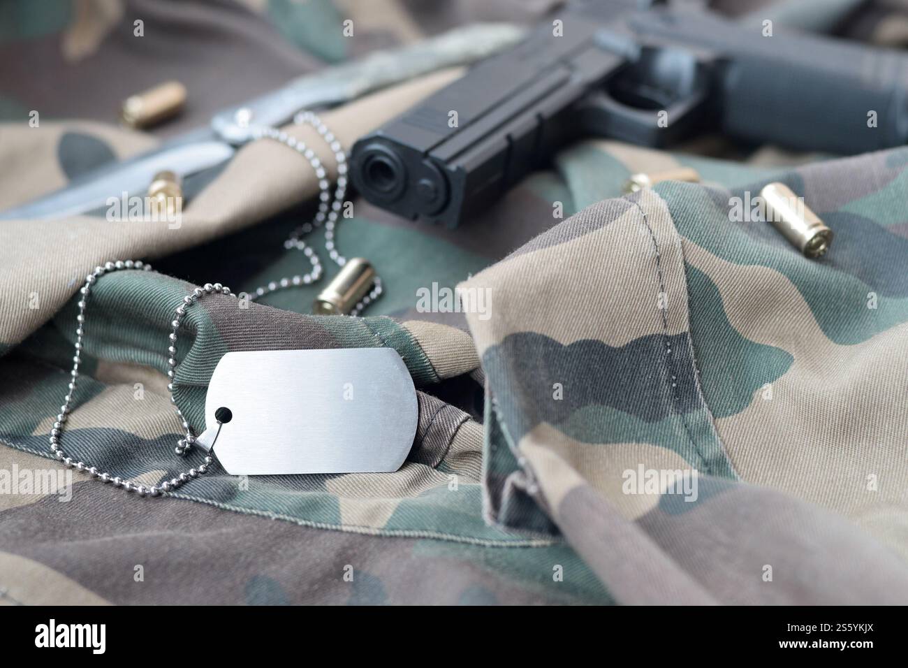 Army Dog tag token with 9mm bullets and pistol lie on folded camouflage ...