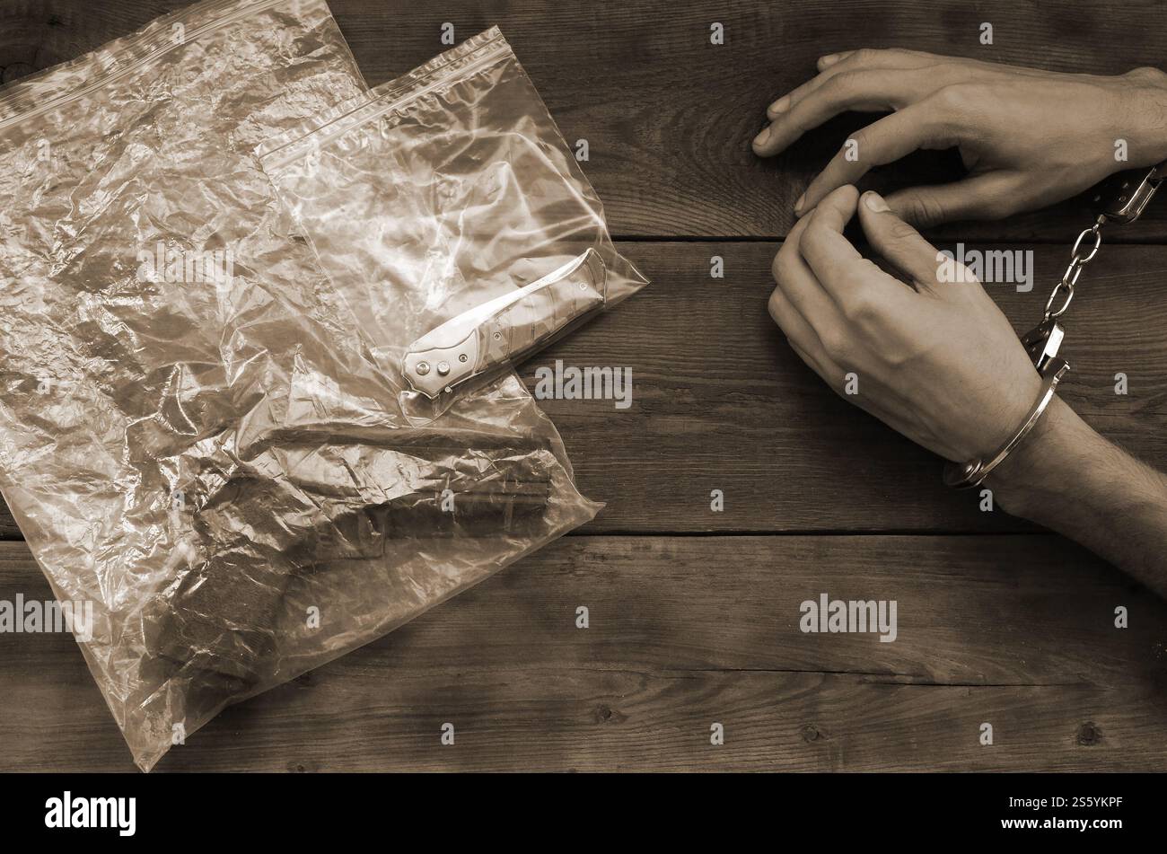 Handcuffed hands of criminal suspect on wooden table and crime scene ...