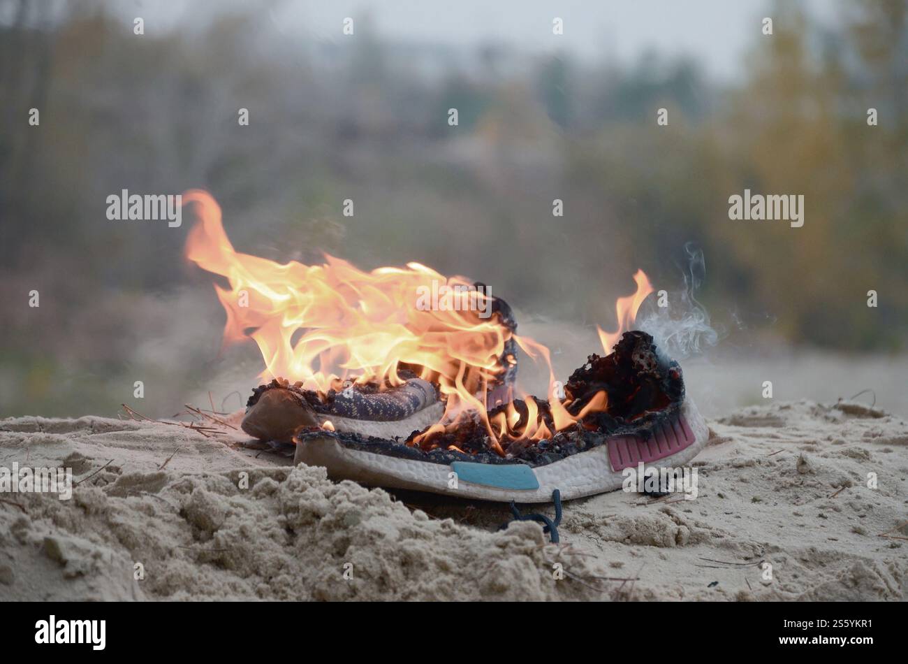 Burning sports sneakers or gym shoes on fire stand on sandy beach coast ...