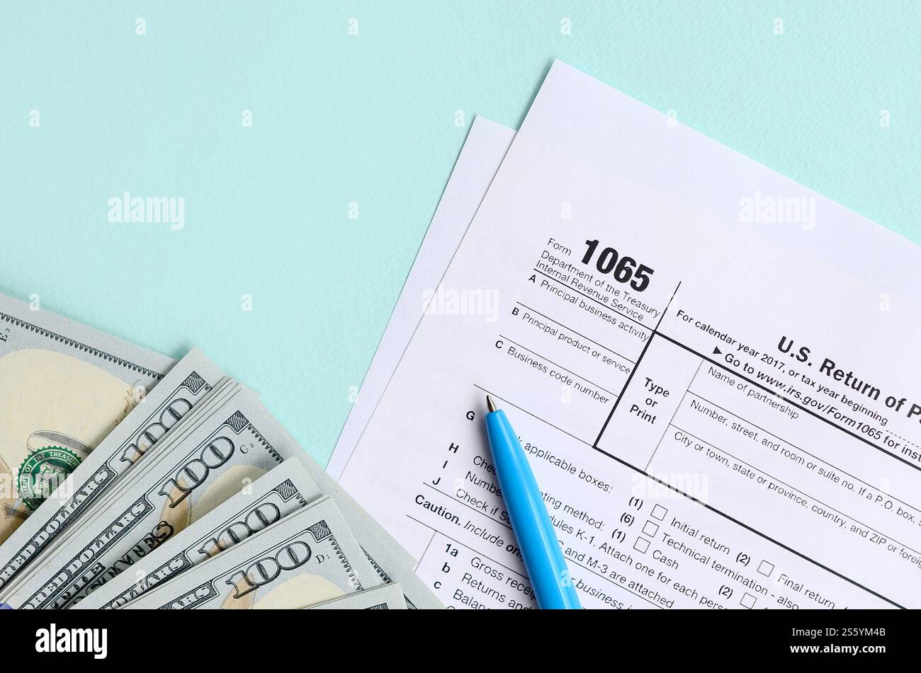 1065 tax form lies near hundred dollar bills and blue pen on a light ...