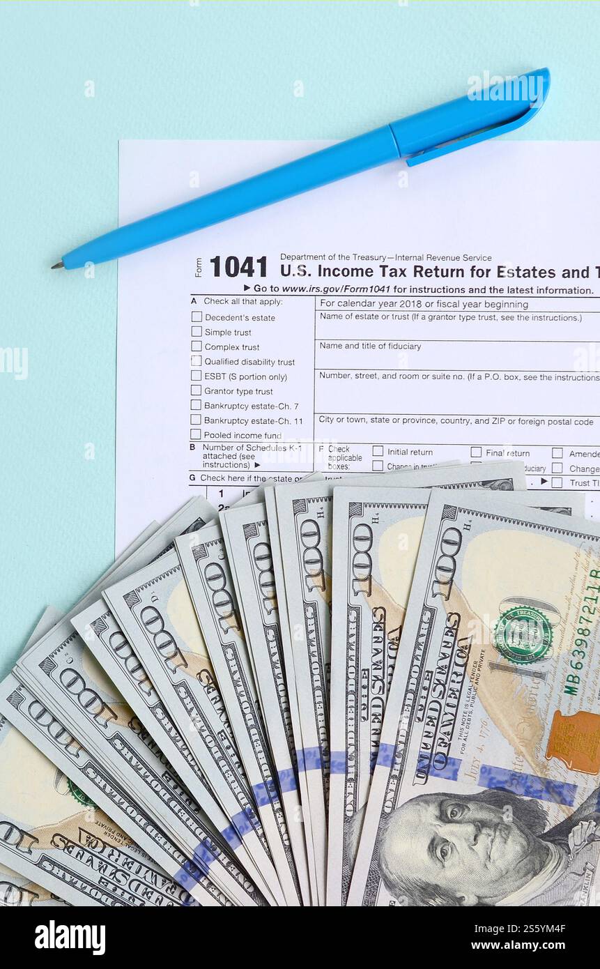 1041 tax form lies near hundred dollar bills and blue pen on a light blue background. US Income ...