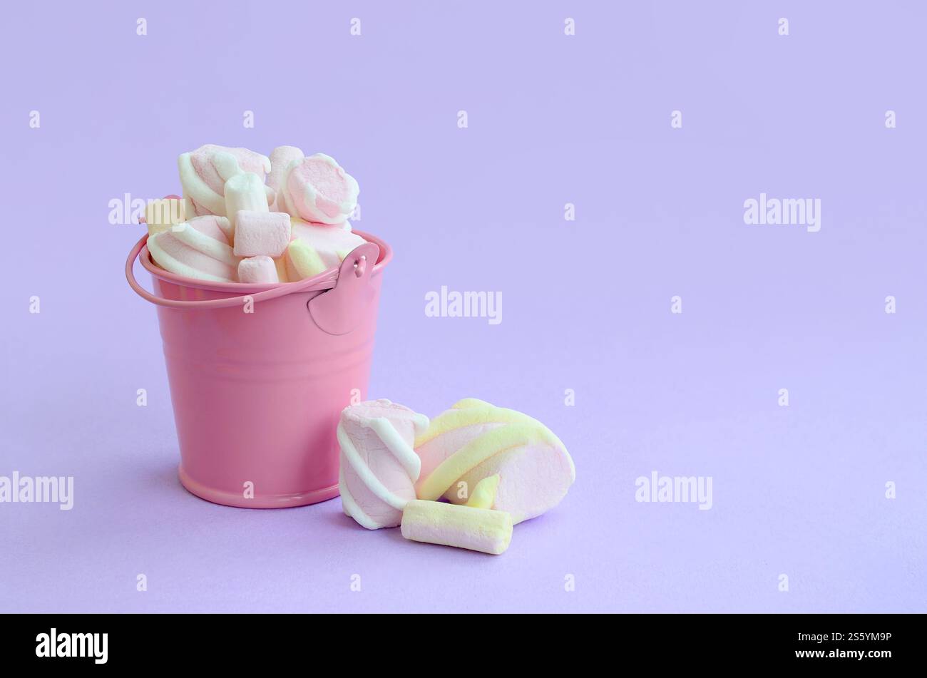 A miniature pink bucket filled with marshmallow lies on a violet pastel ...