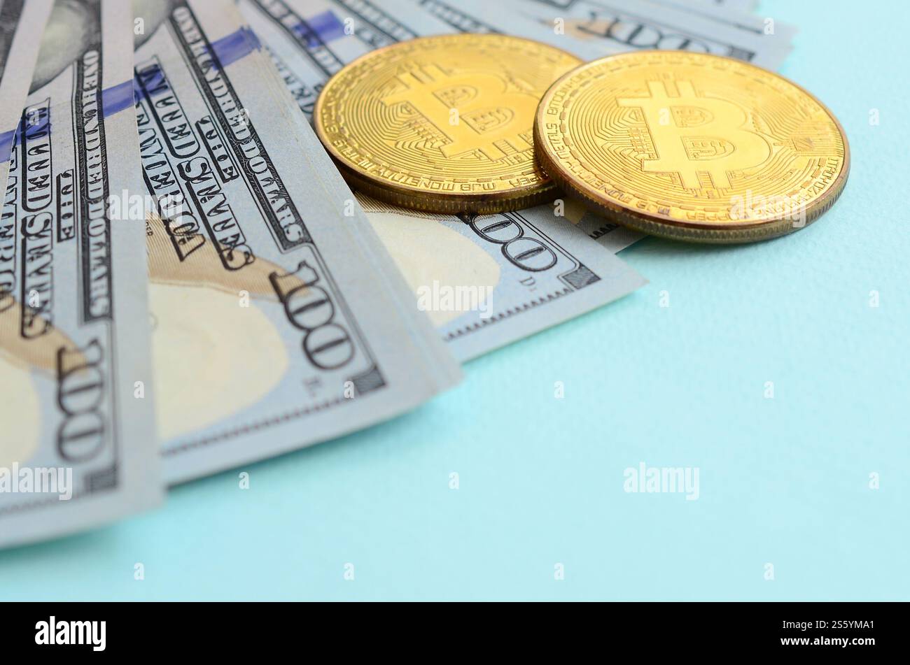 Golden bitcoins and hundred dollar bills lies on light blue background ...