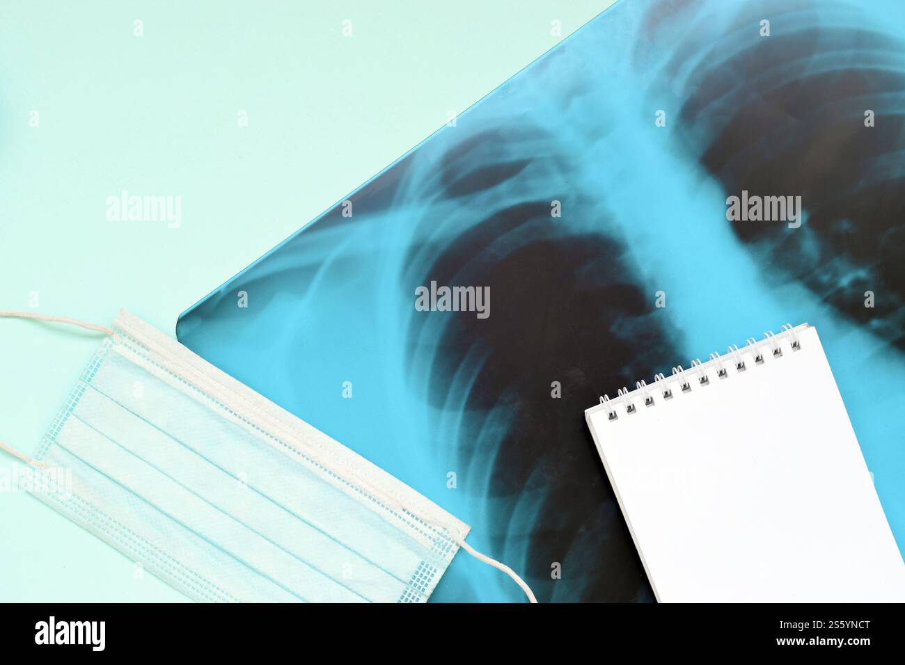 Respiratory mask and empty notepad page on x-ray of human lungs, top ...