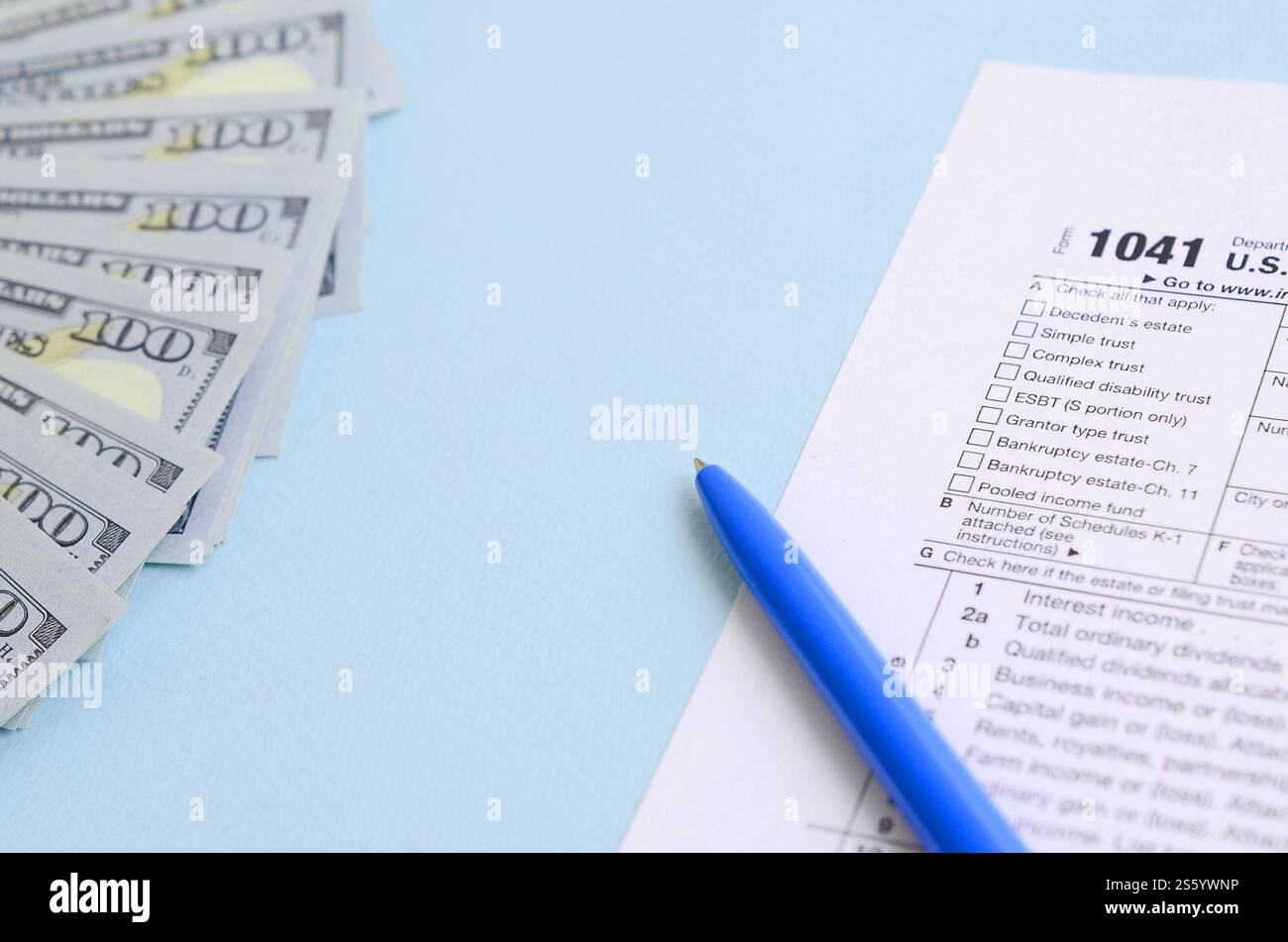 1041 tax form lies near hundred dollar bills and blue pen on a light ...