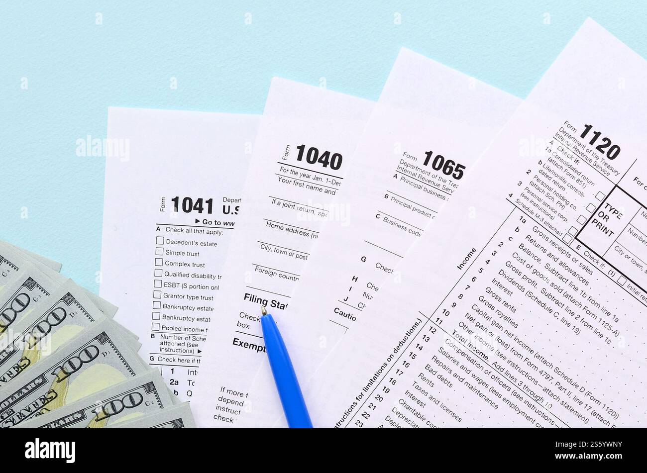 Tax forms lies near hundred dollar bills and blue pen on a light blue ...