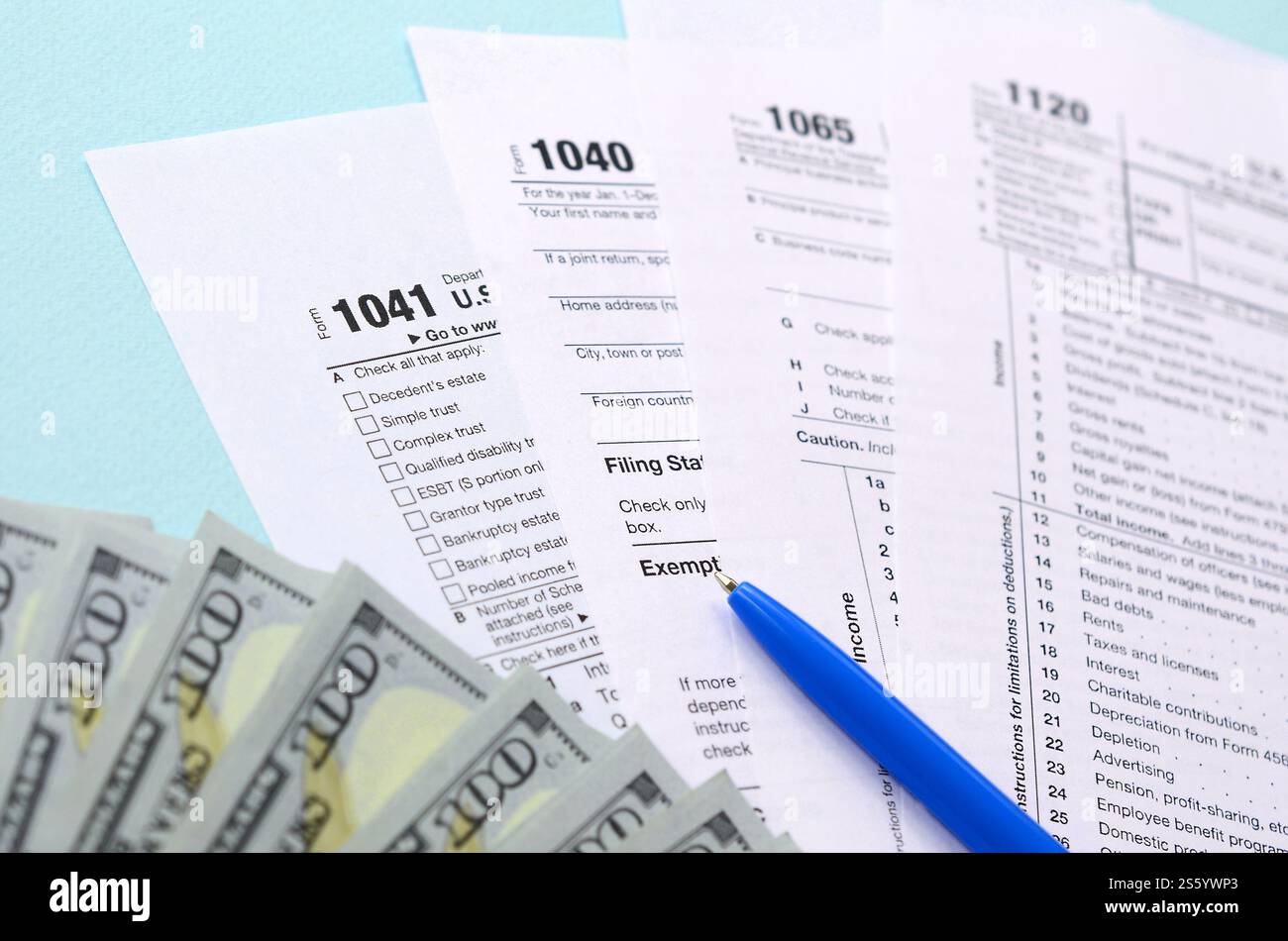 Tax forms lies near hundred dollar bills and blue pen on a light blue ...