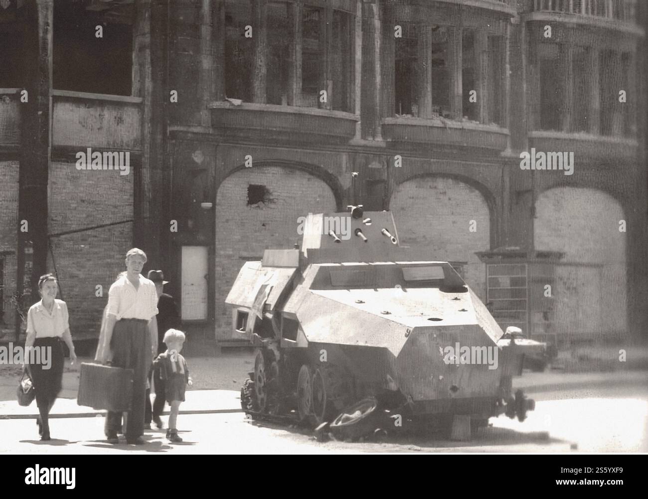 family of civilians with suitcases walking past a destroyed SdKfz 251 ...