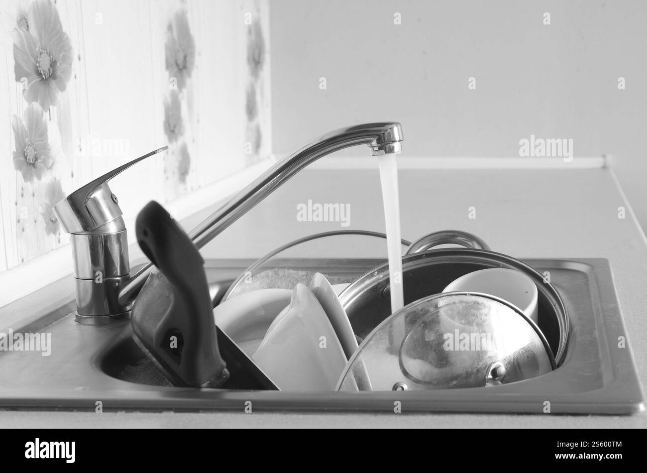 Dirty dishes and unwashed kitchen appliances lie in foam water under a ...