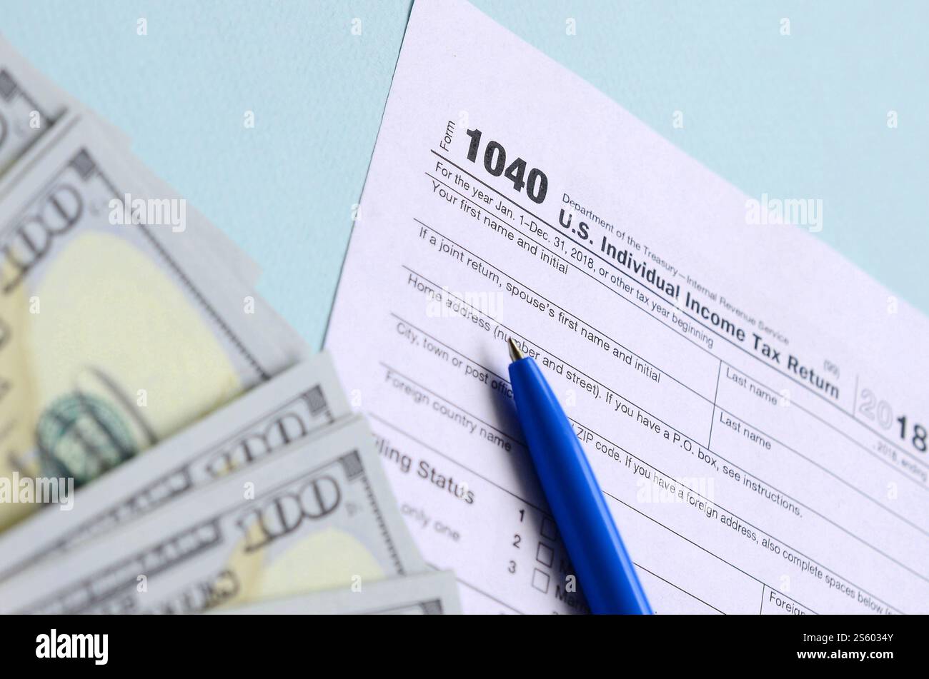 1040 tax form lies near hundred dollar bills and blue pen on a light ...