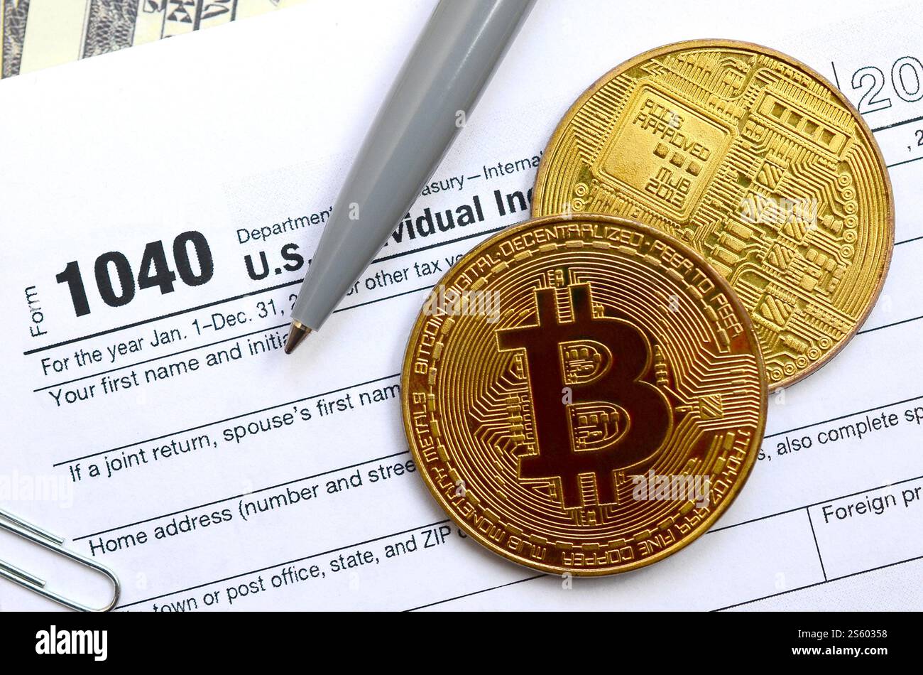 The pen, bitcoins and dollar bills is lies on the tax form 1040 U.S ...