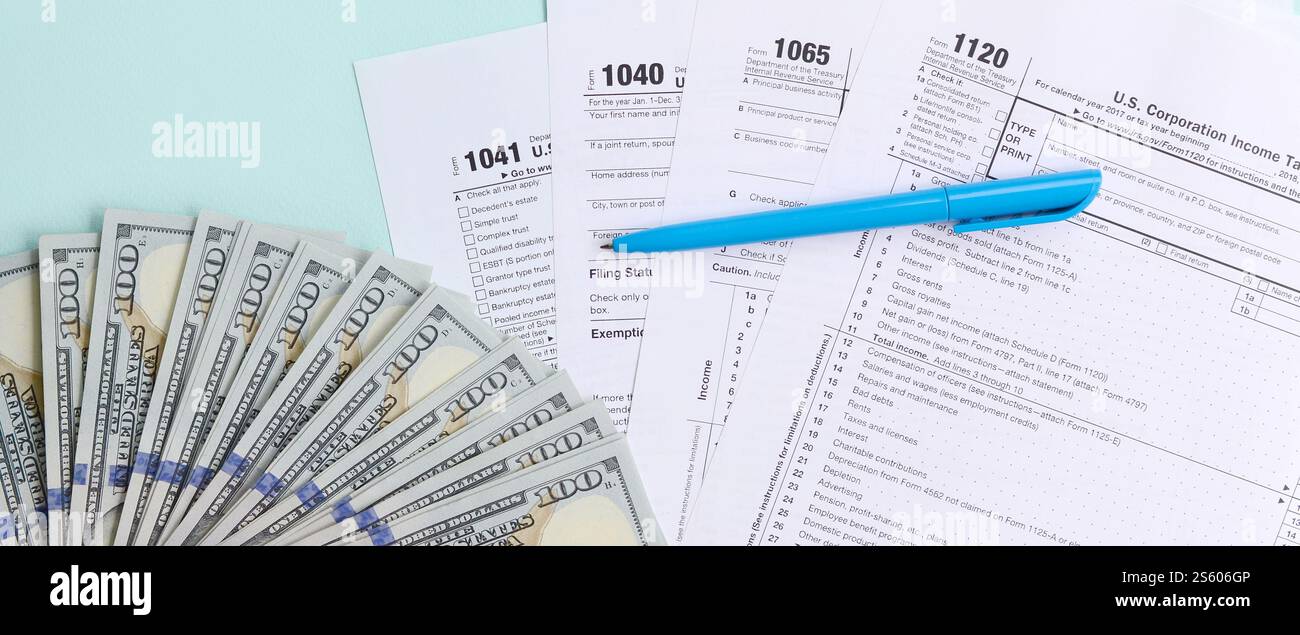 Tax forms lies near hundred dollar bills and blue pen on a light blue ...