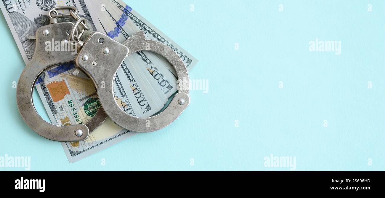 Silver police handcuffs and hundred dollar bills lies on light blue ...