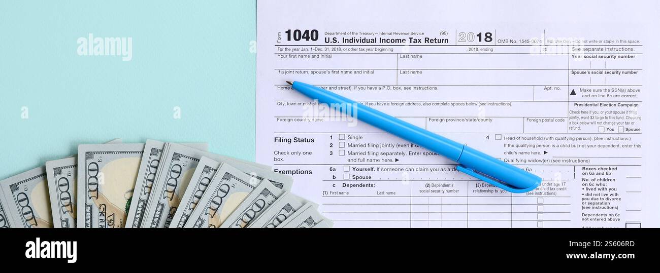 1040 tax form lies near hundred dollar bills and blue pen on a light ...