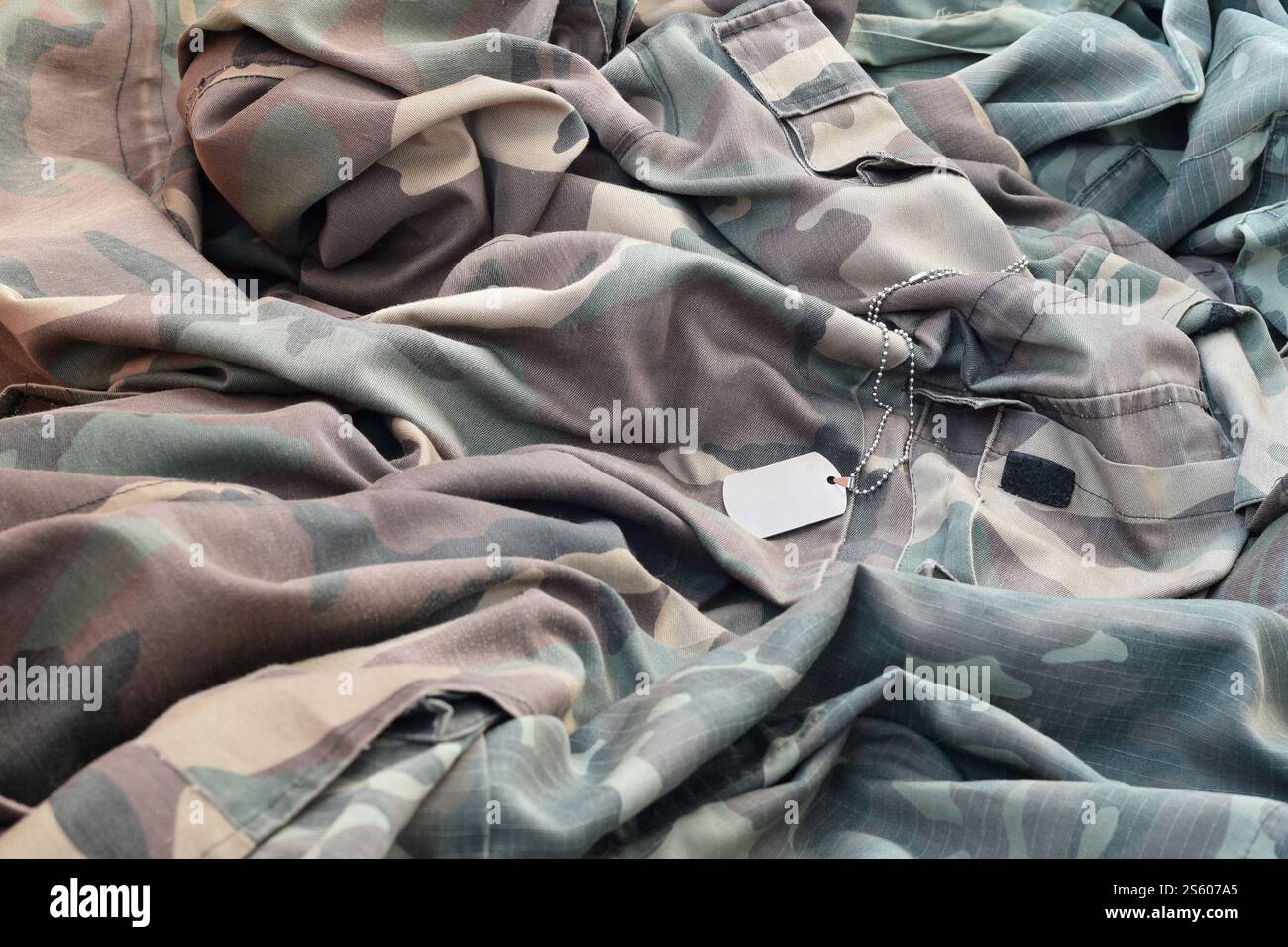 Lost and empty army dog tag lies on pile of folded camouflage clothes ...