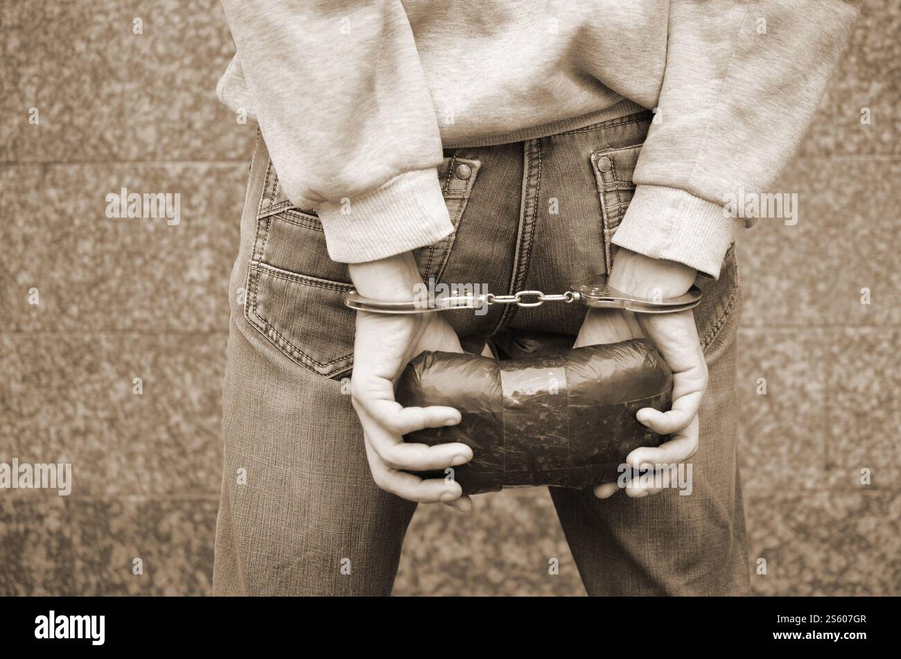 Arrested drug dealer in handcuffs with big heroin drug package on dark ...