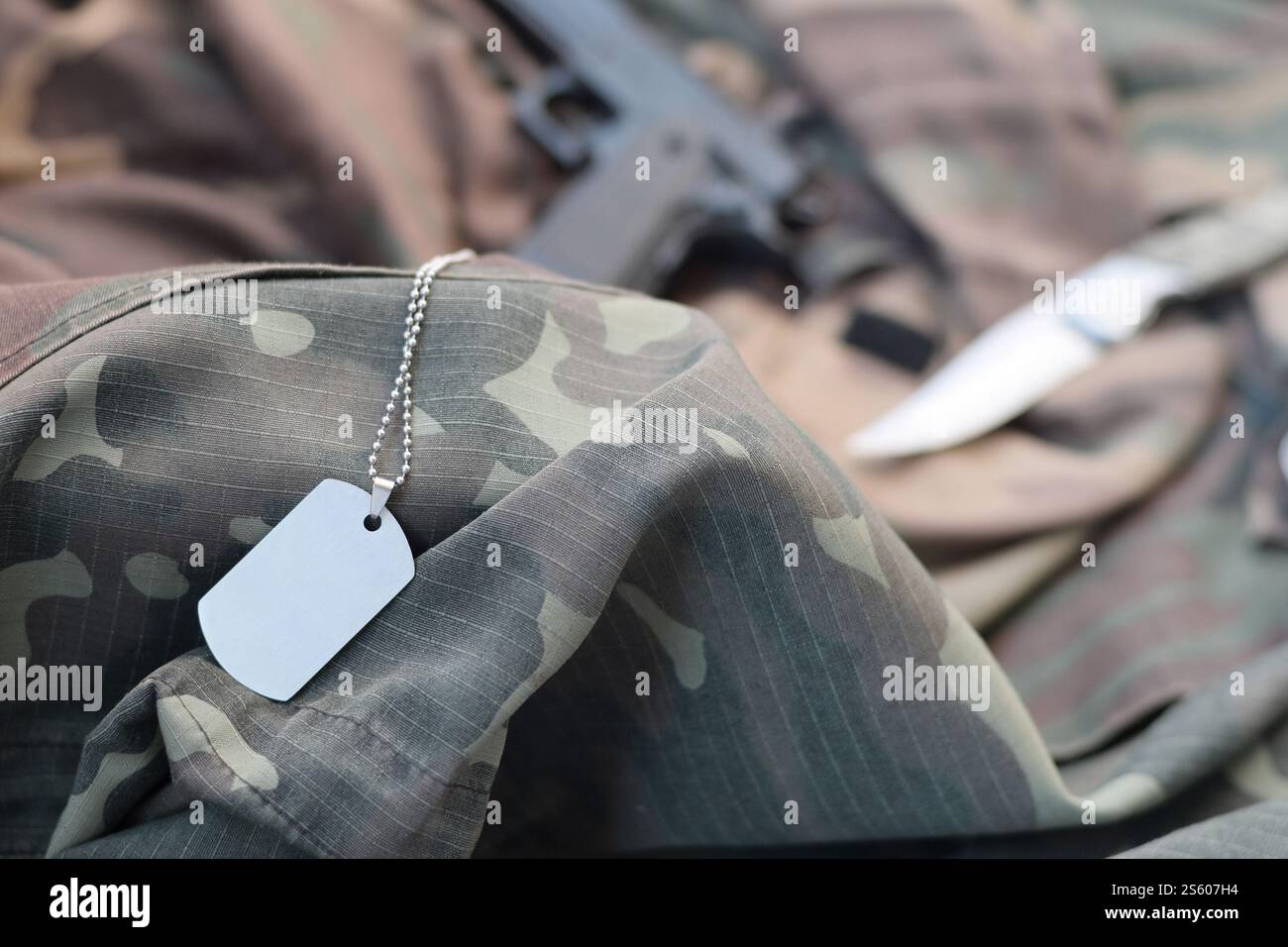 Army Dog tag token with Knife and pistol lie on folded camouflage green ...