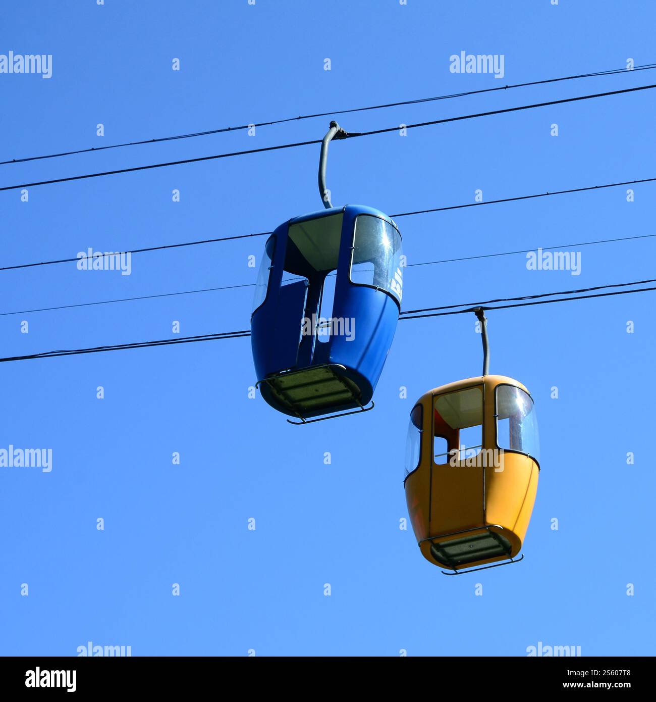 Blue and yellow passenger cable way cabins in the clear blue sky. Blue ...