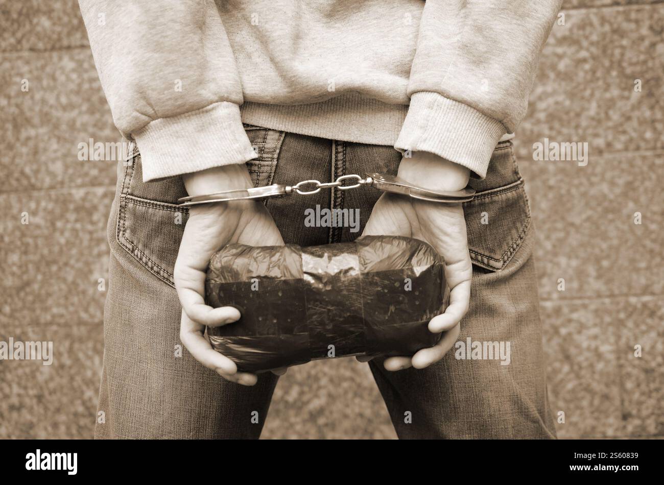 Arrested drug dealer in handcuffs with big heroin drug package on dark ...