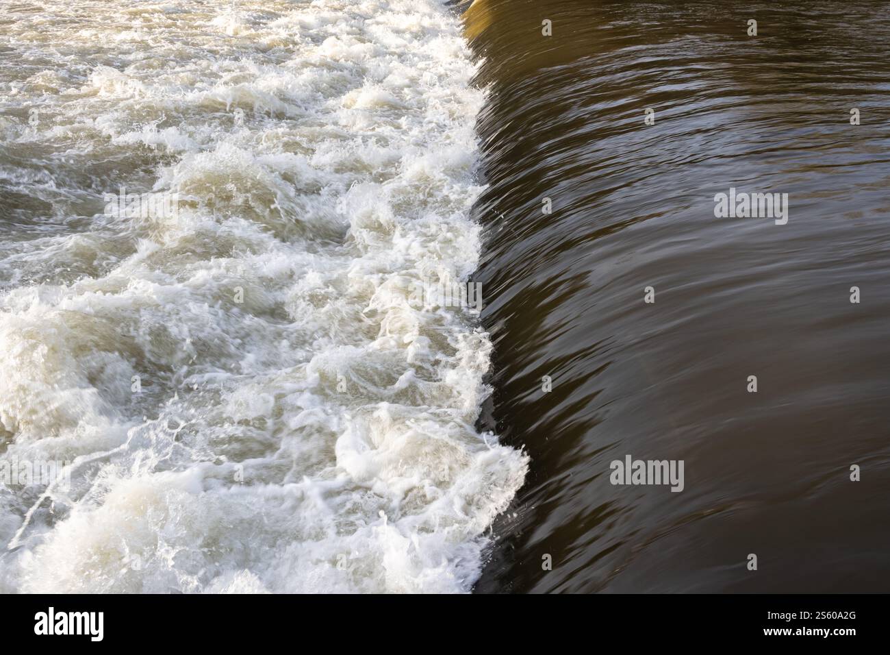 Clean water flowing into polluted river creating foam, waves and a ...