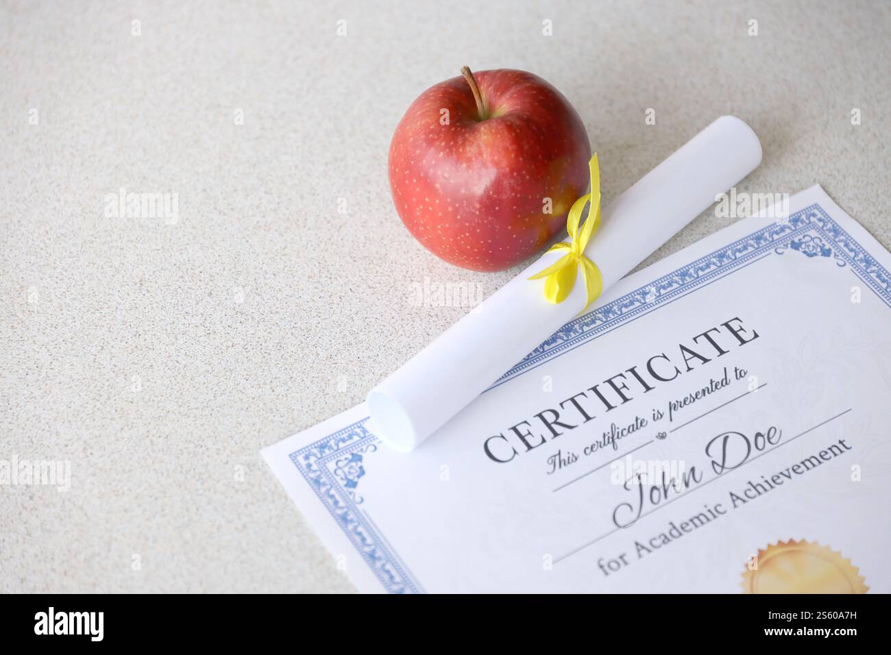 A certificate of achievement lies on table with small scroll and red ...
