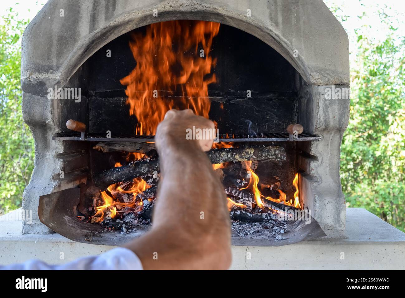Hand keeps fire going in a grill with fiery flames - an empty fire ...