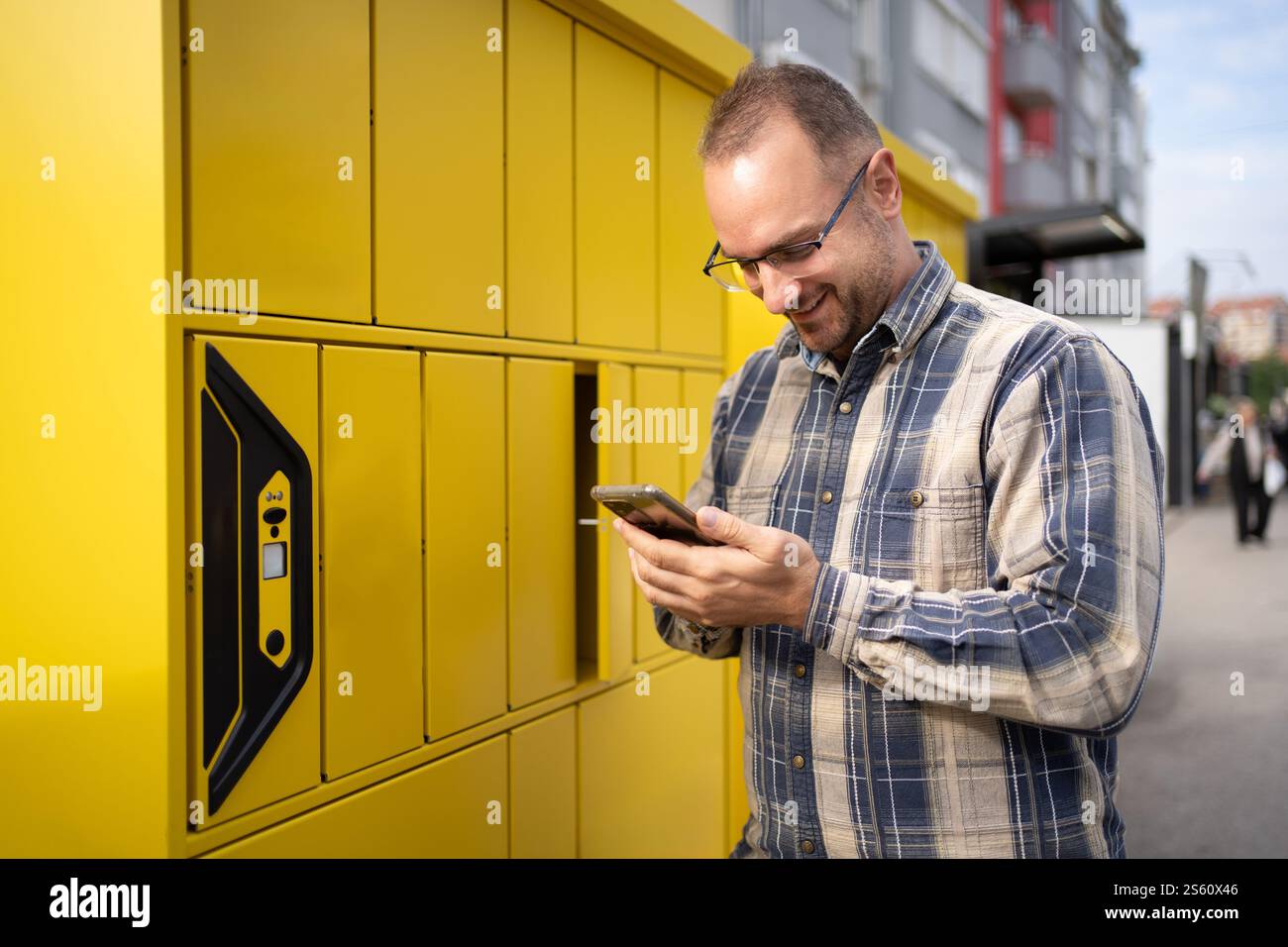 Happy man collects package from bright yellow locker in urban setting ...