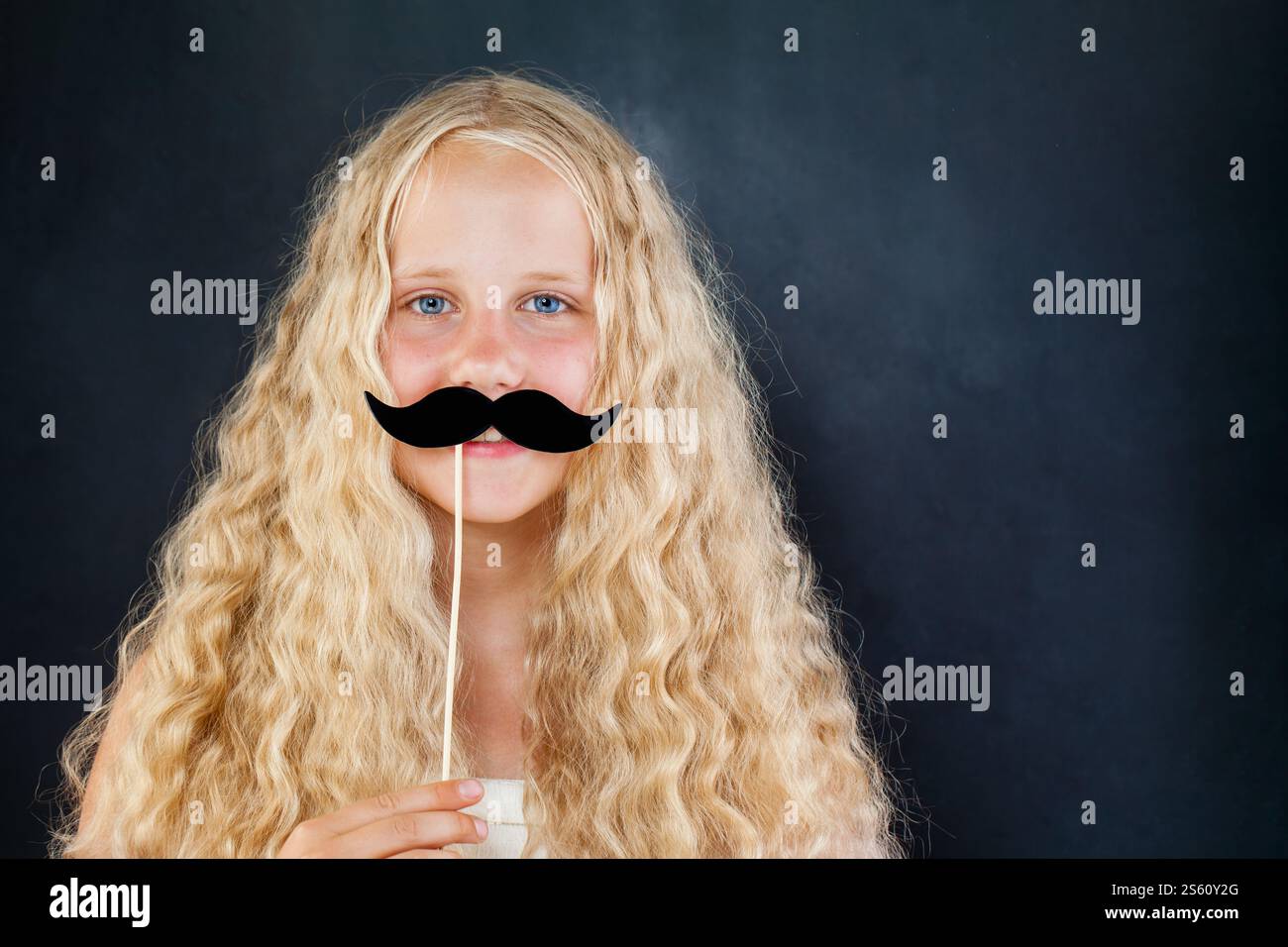 Pretty young girl posing with photo booth props mustache on black ...