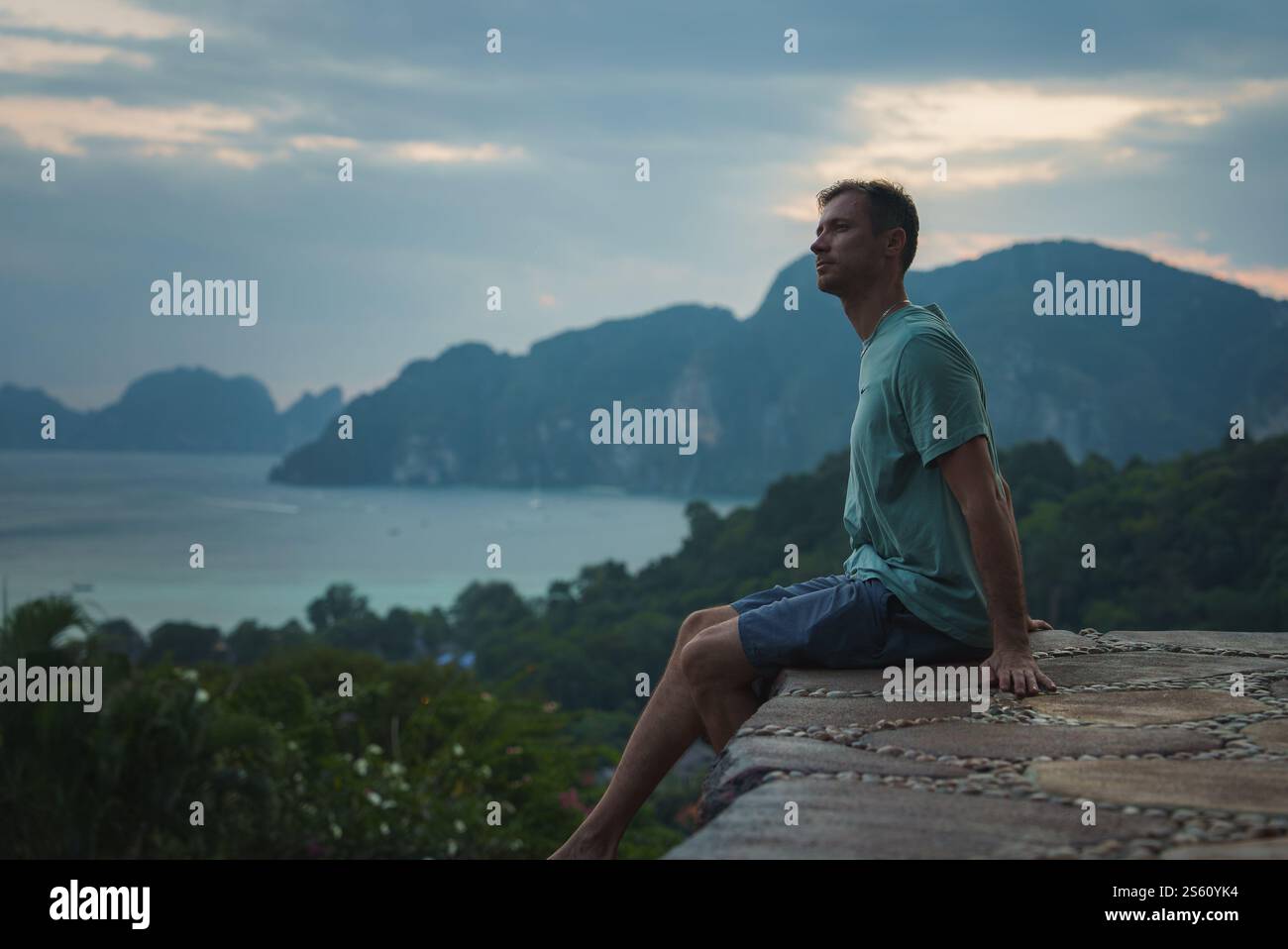 Man Sitting on Ledge Overlooking Coastal Landscape in Thailand Stock ...