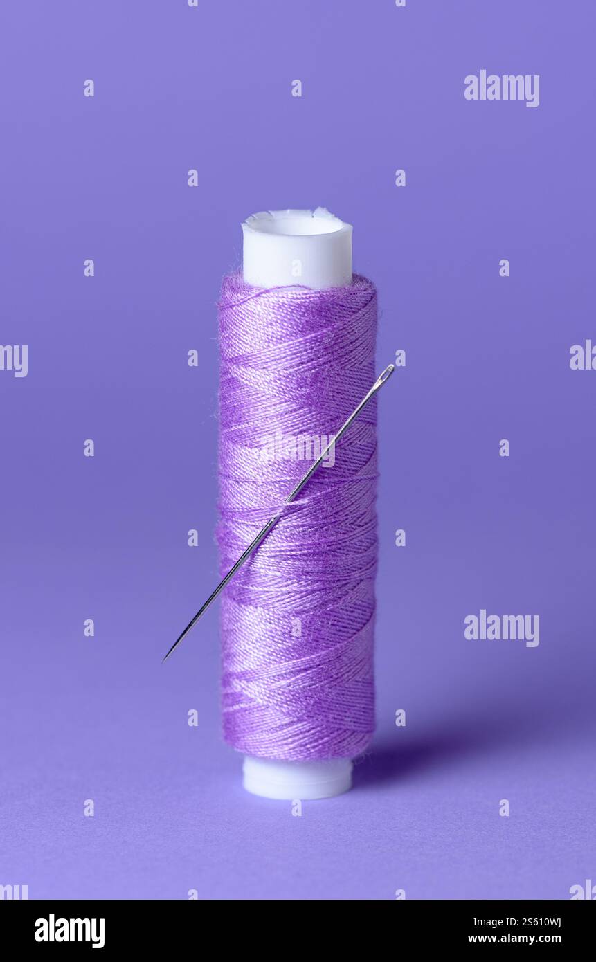 Purple violet thread spool with needle close-up flat lay top view ...