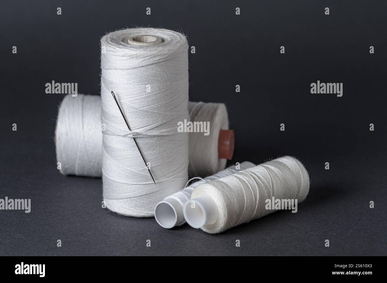 White thread spools with needle on black background with copy space for ...