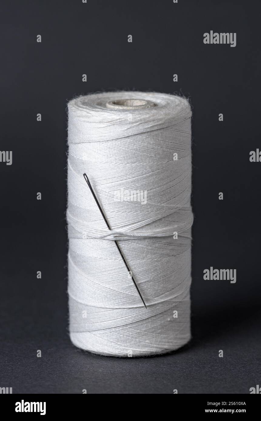 White thread spool with needle close-up flat lay top view on black ...