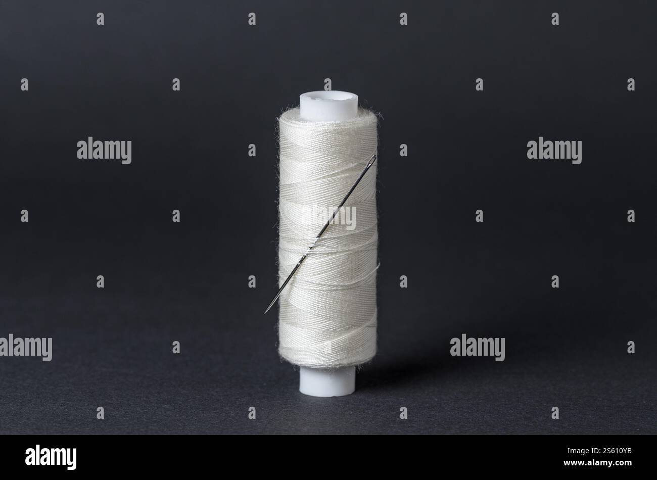 White thread spool with needle close-up flat lay top view on black ...