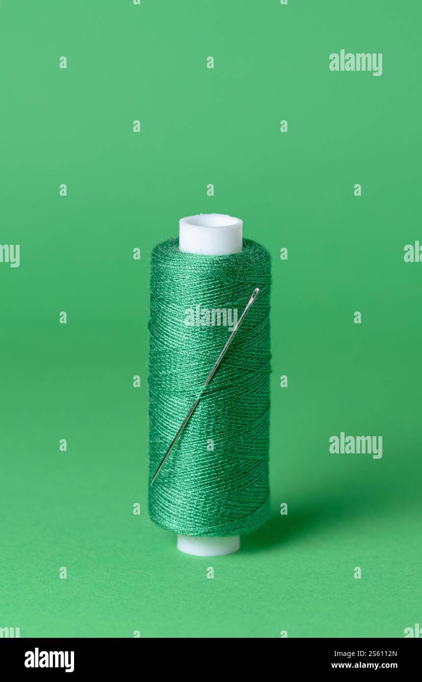 Green thread spool with needle close-up flat lay top view background ...