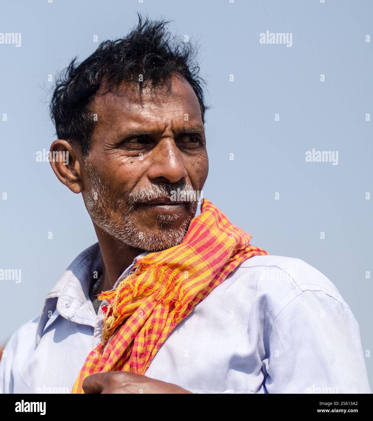 Man in traditional attire sitting outdoors against a weathered wall in ...