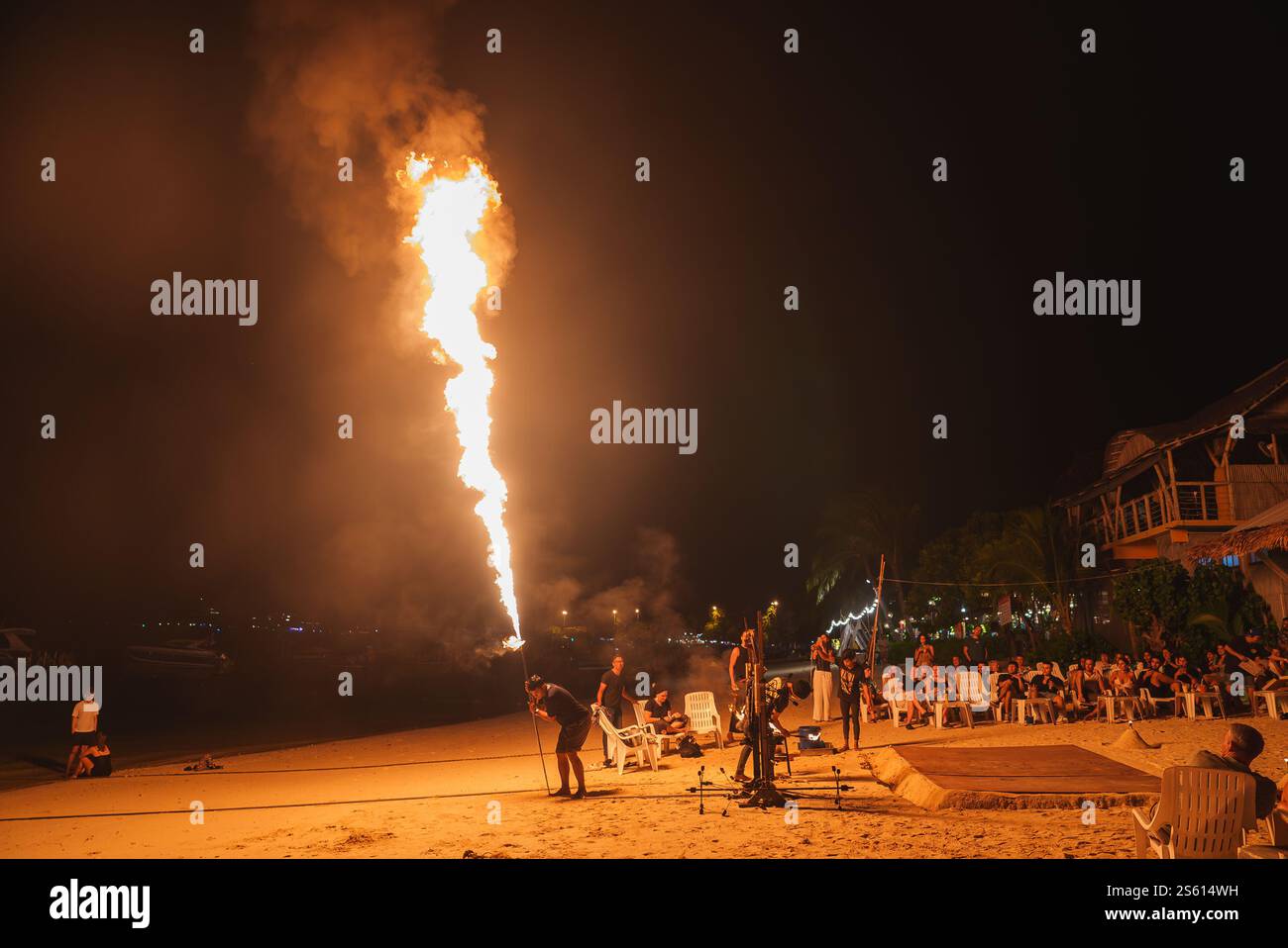 A fire performer creates a towering flame on a sandy beach at night ...