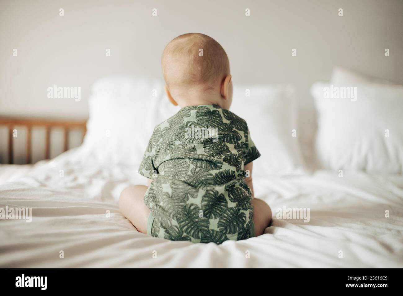 Baby, back view and infant sitting on a bed in a bedroom relax in ...