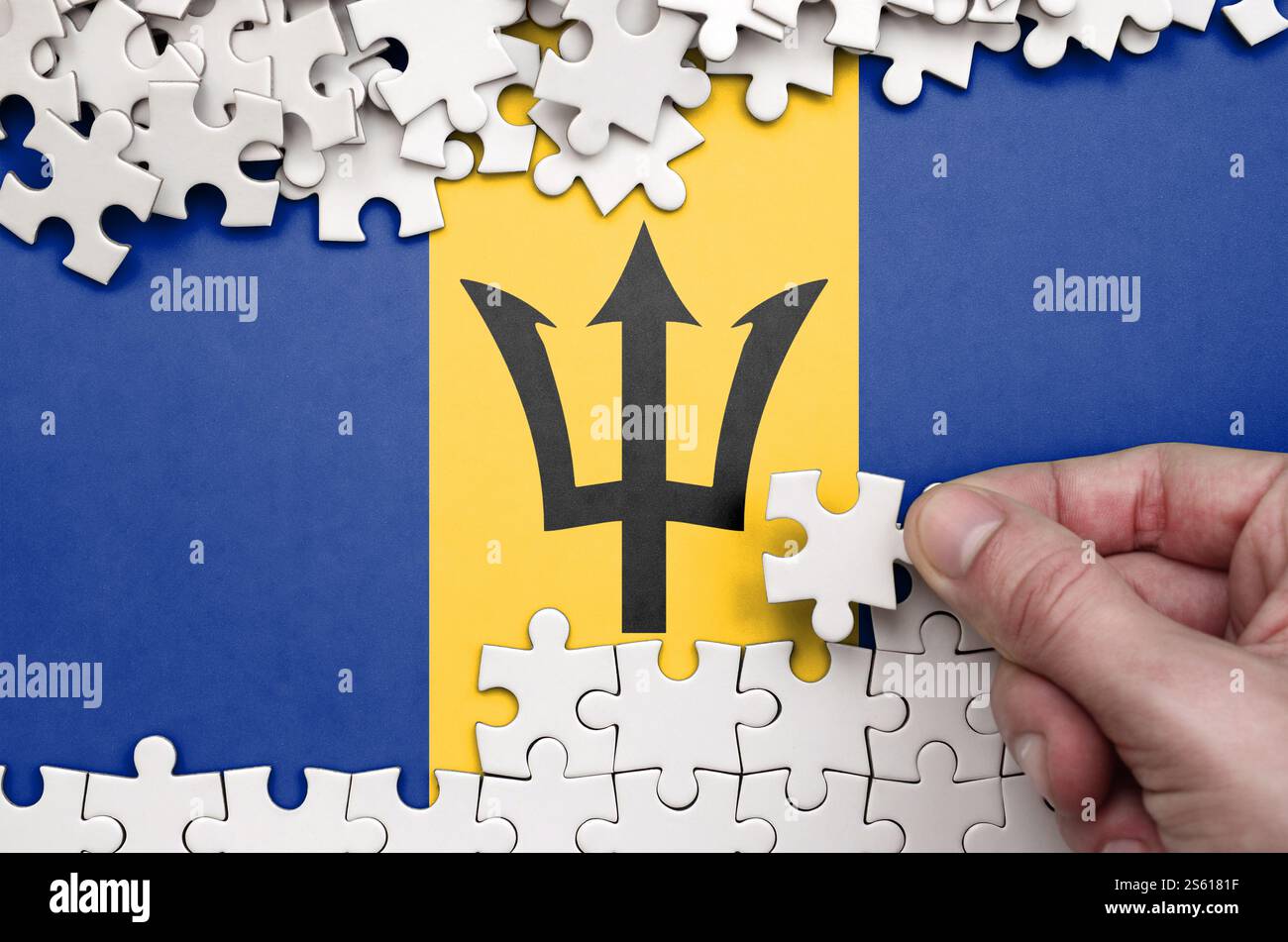 Barbados flag is depicted on a table on which the human hand folds a ...