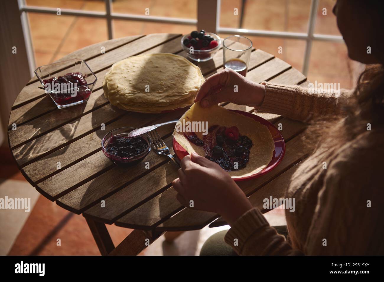 A cozy breakfast scene of a person making crepes with jam and fresh ...
