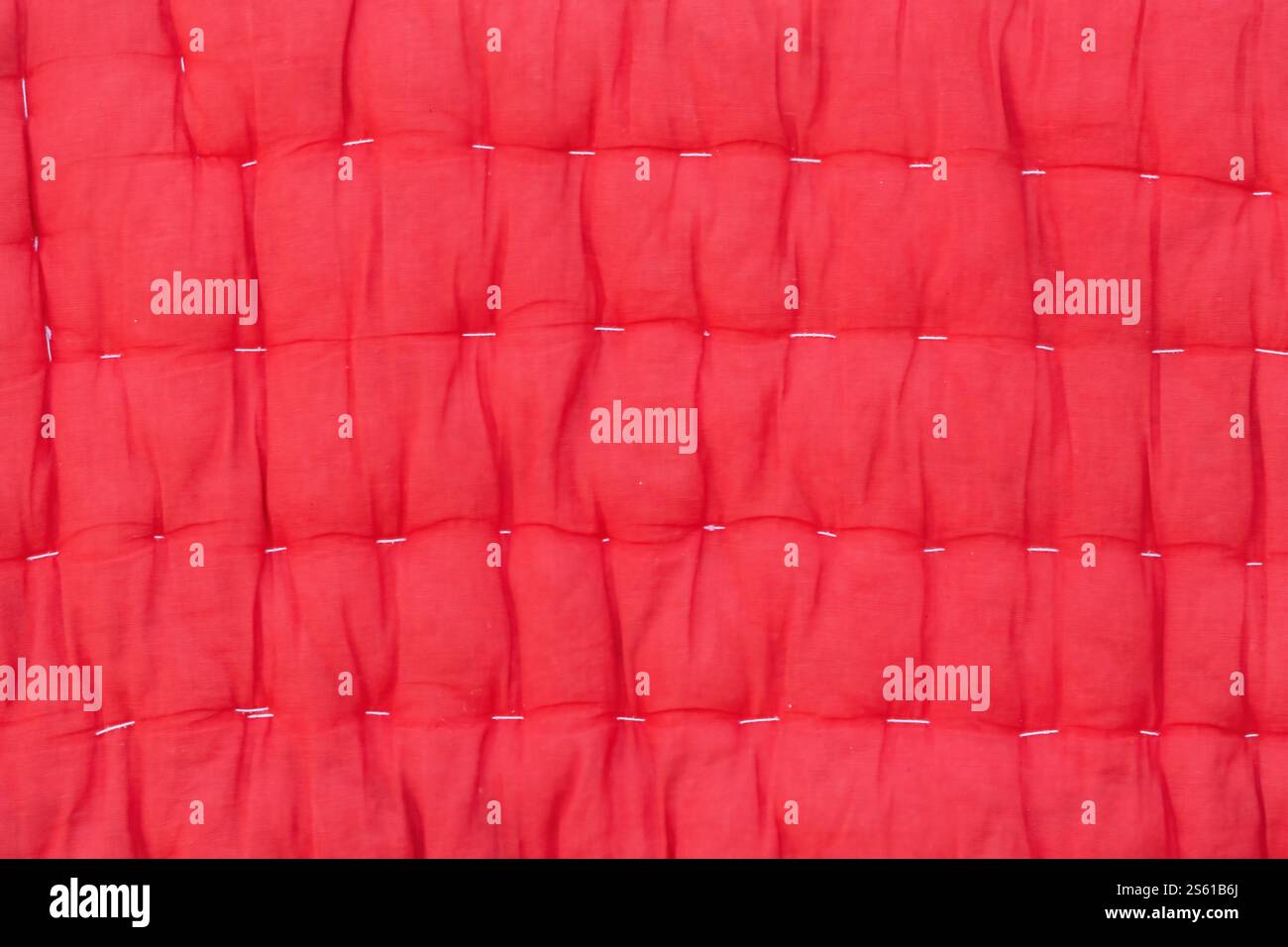 Red fabric background with white thread stitching, showcasing the ...