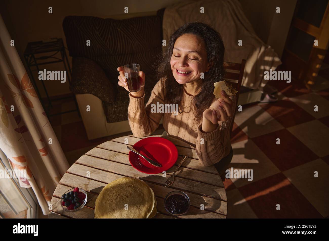 A cheerful woman sits at a cozy table savoring crepes, berries, and a ...