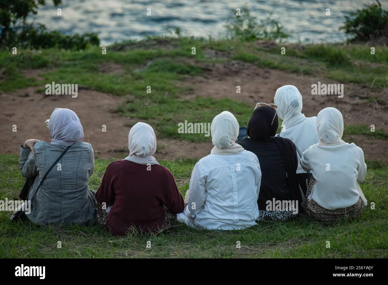 Back view of the muslim women relaxing on green grass in the nature ...