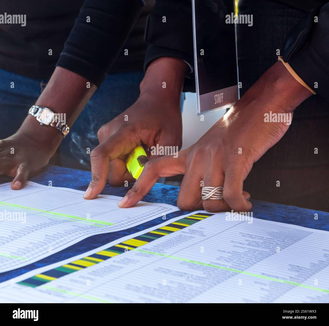 african hands pointing fingers at a paper list, staff members counting ...