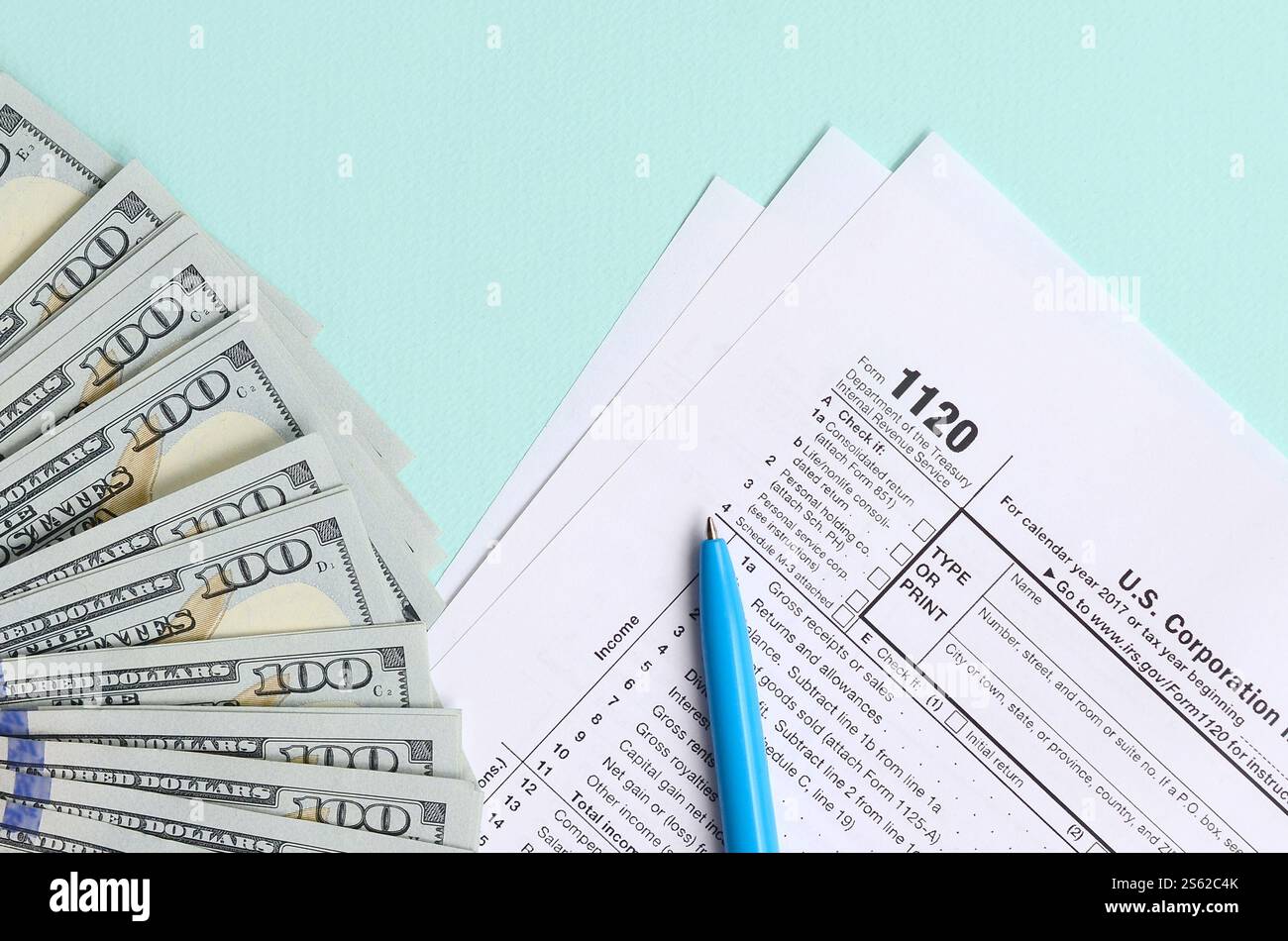 1120 tax form lies near hundred dollar bills and blue pen on a light ...