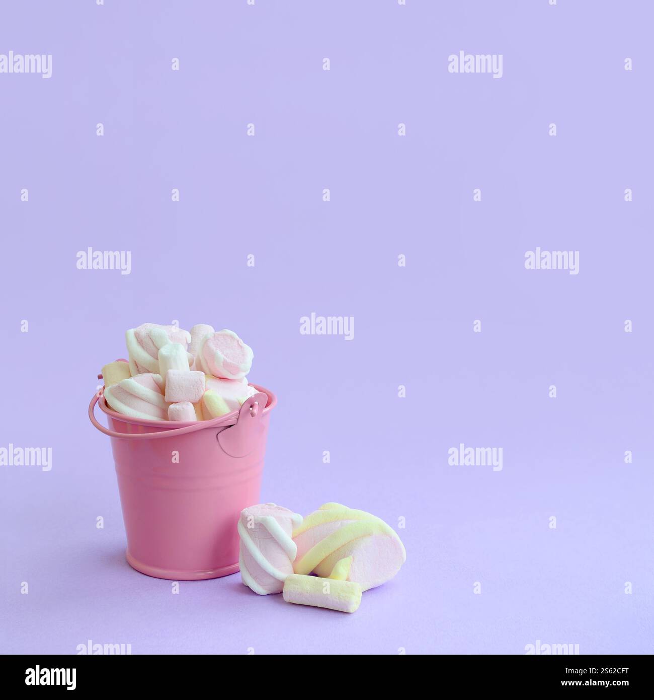 A miniature pink bucket filled with marshmallow lies on a violet pastel ...