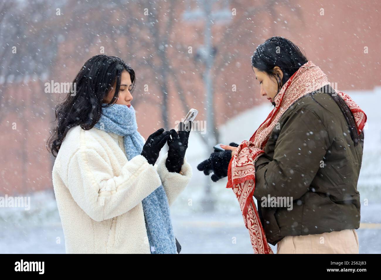 Two girls using smartphones on city street during blizzard, snowfall in ...