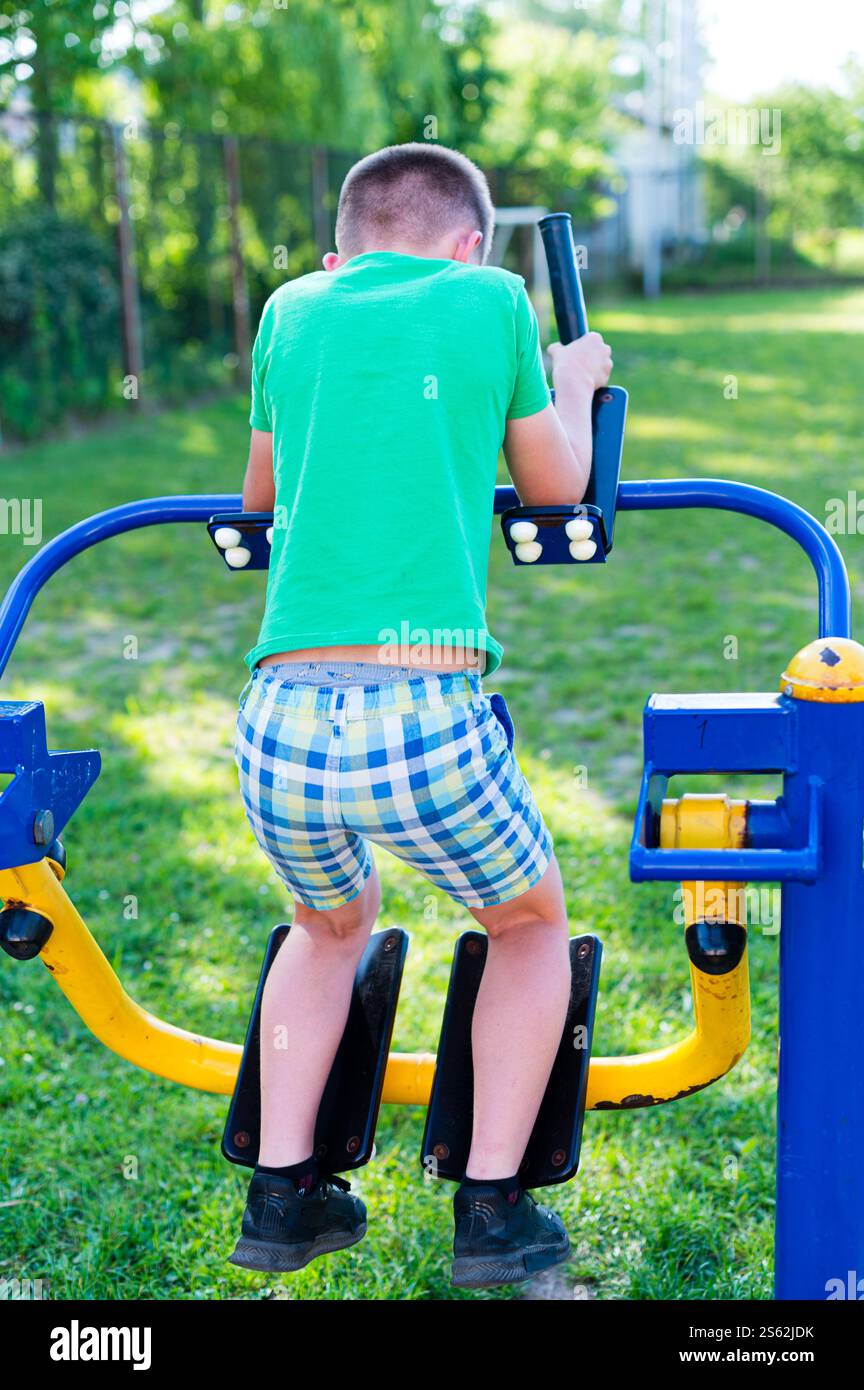 A young boy uses outdoor exercise equipment, strengthening his muscles ...
