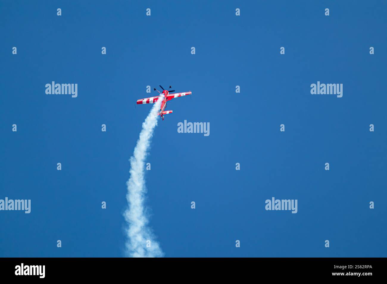 Bright red plane Sukhoi Su-31 upside down stunts with contrails in blue ...